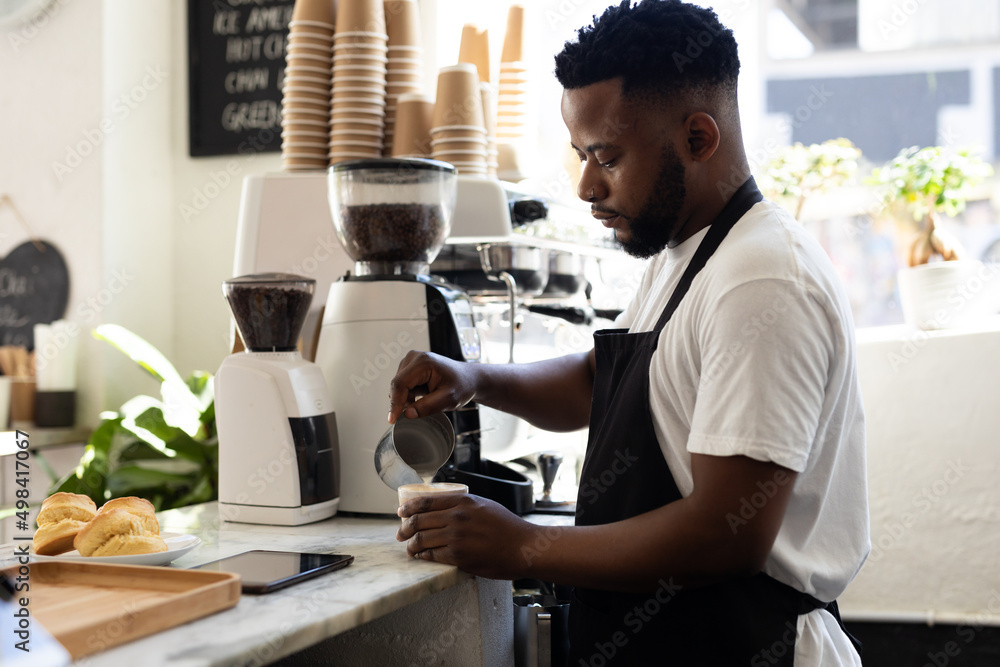 Confident young african american barista adding milk in coffee cup ...