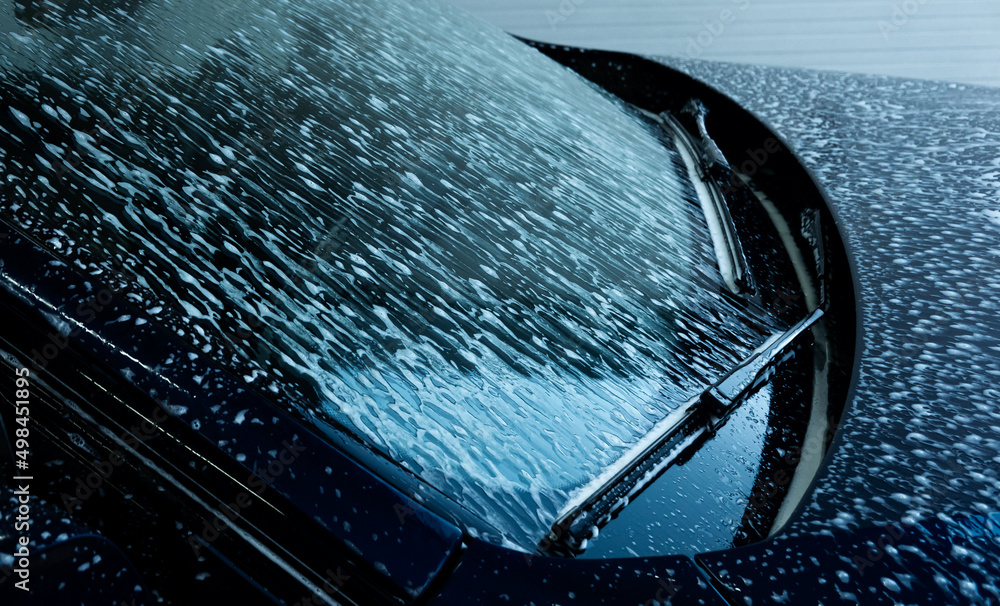 Self-service car wash station. Active foam is cleaning a dirty sedan ...