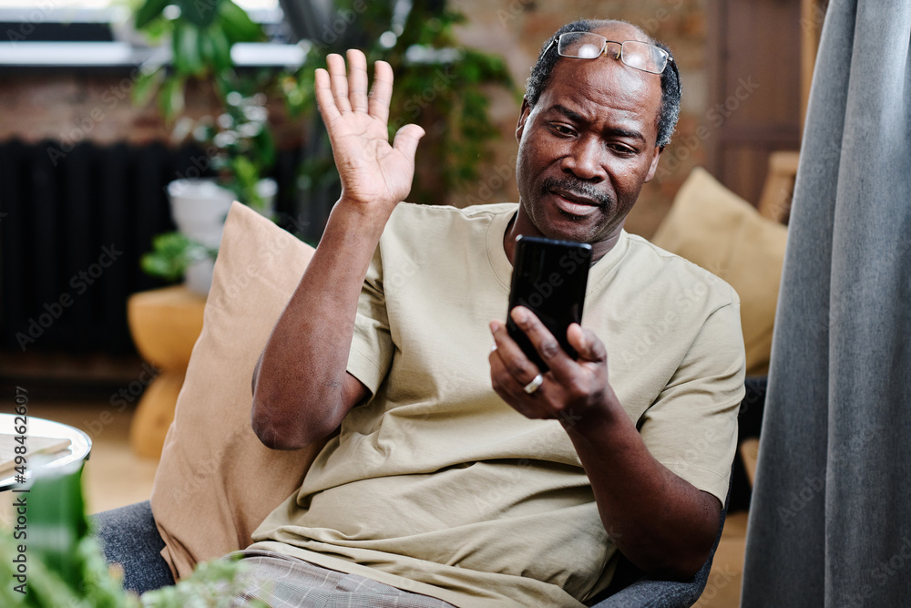 Friendly sernior black man with mobile phone waving hand to someone ...