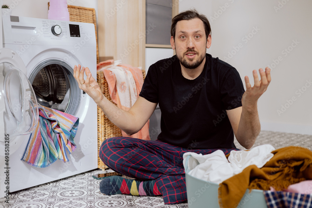 Man is sitting on laundry room floor by open washing machine, throwing ...