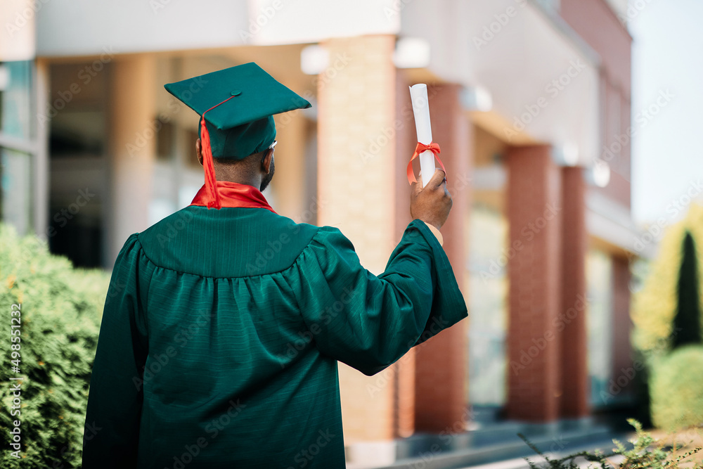 Rear view of black student in graduation gown with college diploma ...