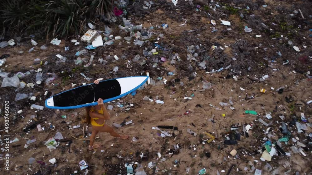 Young female surfer walking barefoot in bikini on polluted beach with ...