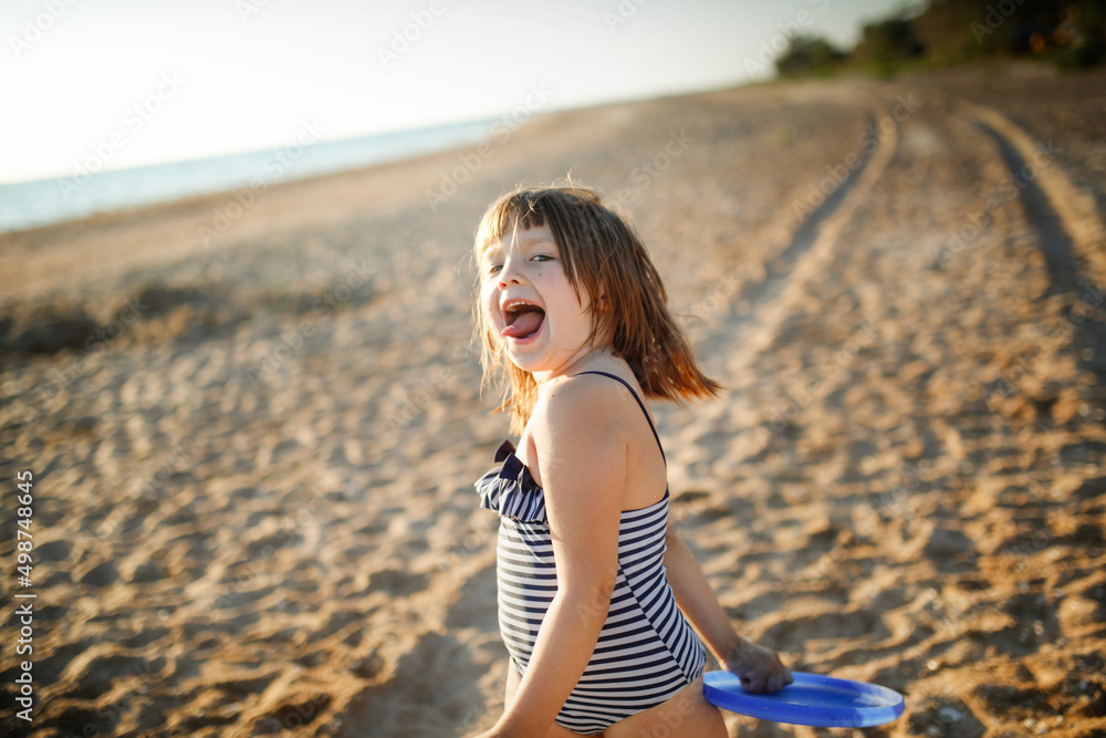 Cute european child girl in a swimsuit runs on the sand and plays ...