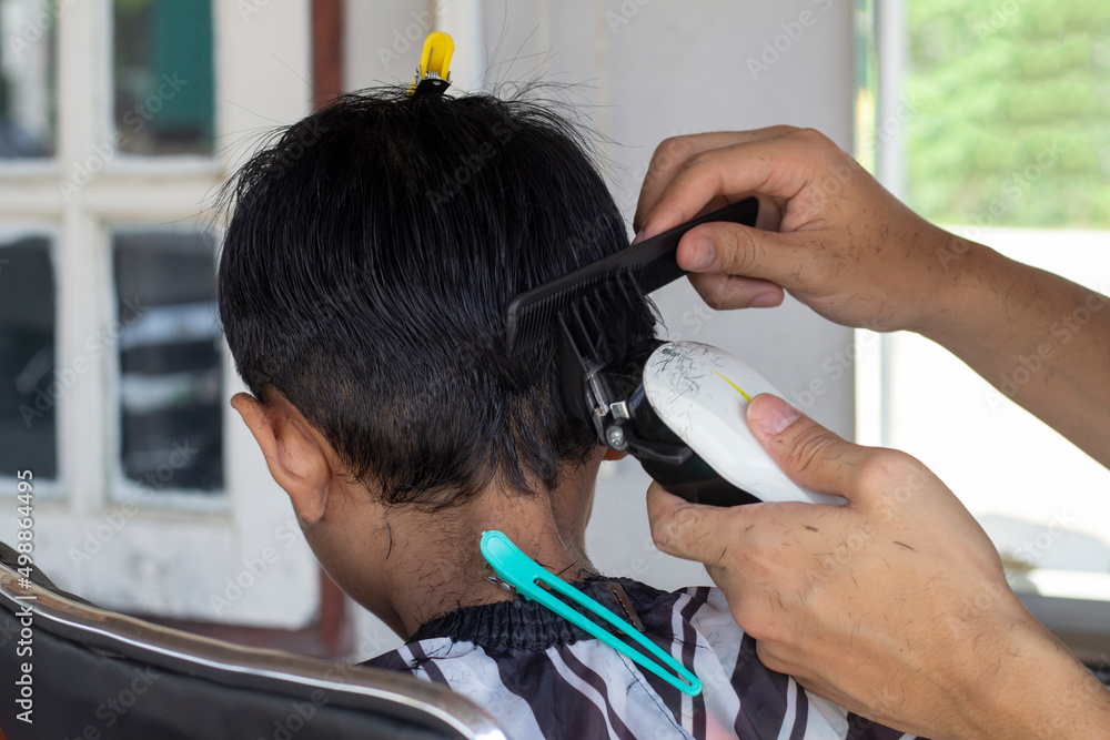 Foto de Hairdresser holding hair clipper for haircutting asian boy in ...