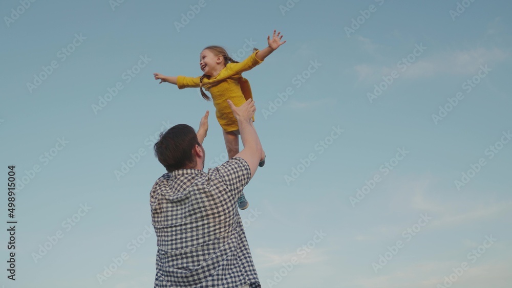 father throws little cheerful child into blue sky. kid laughs with his ...