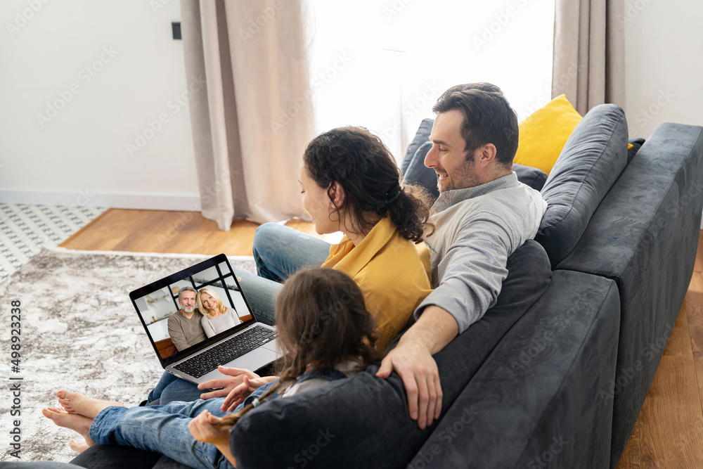 Family of four using laptop for video connection with grandparents or ...