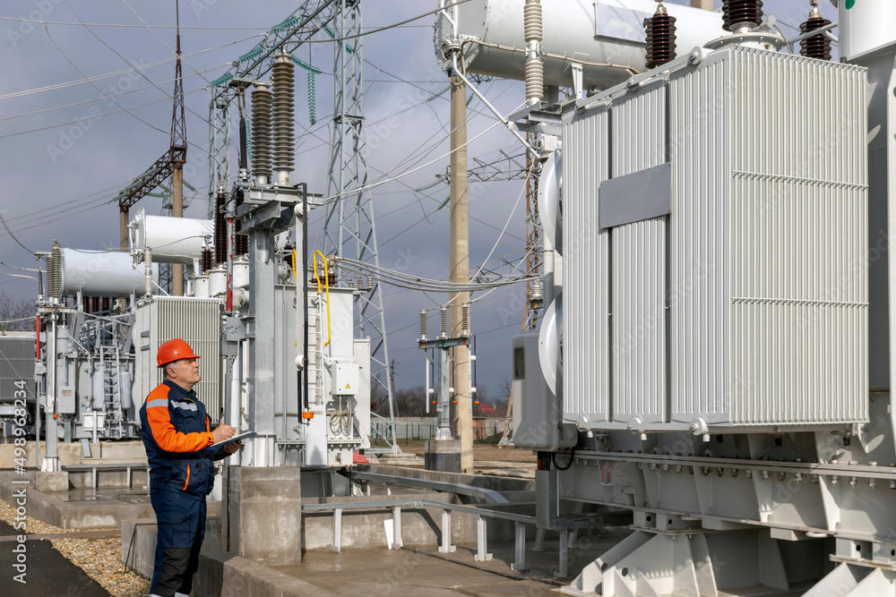 Electrical substation engineer inspects modern high-voltage equipment ...