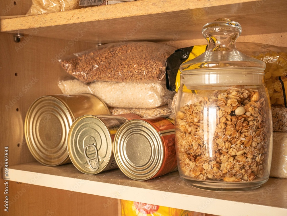 Shelf in the kitchen cabinet with packs of different cereals and canned ...