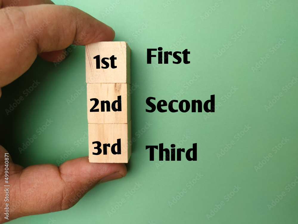 Hand holding wooden block with text First Second Third on green ...