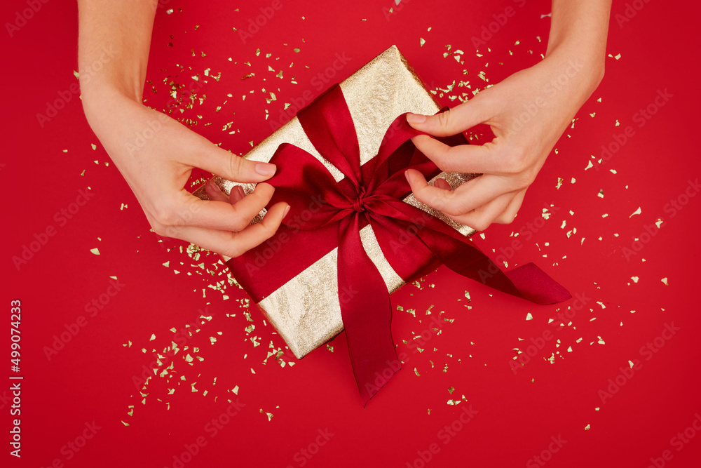 Female hands tying a bow on gift box with a red ribbon on wine ...
