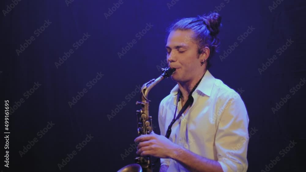 Saxophonist playing his instrument under blue lights, black background ...