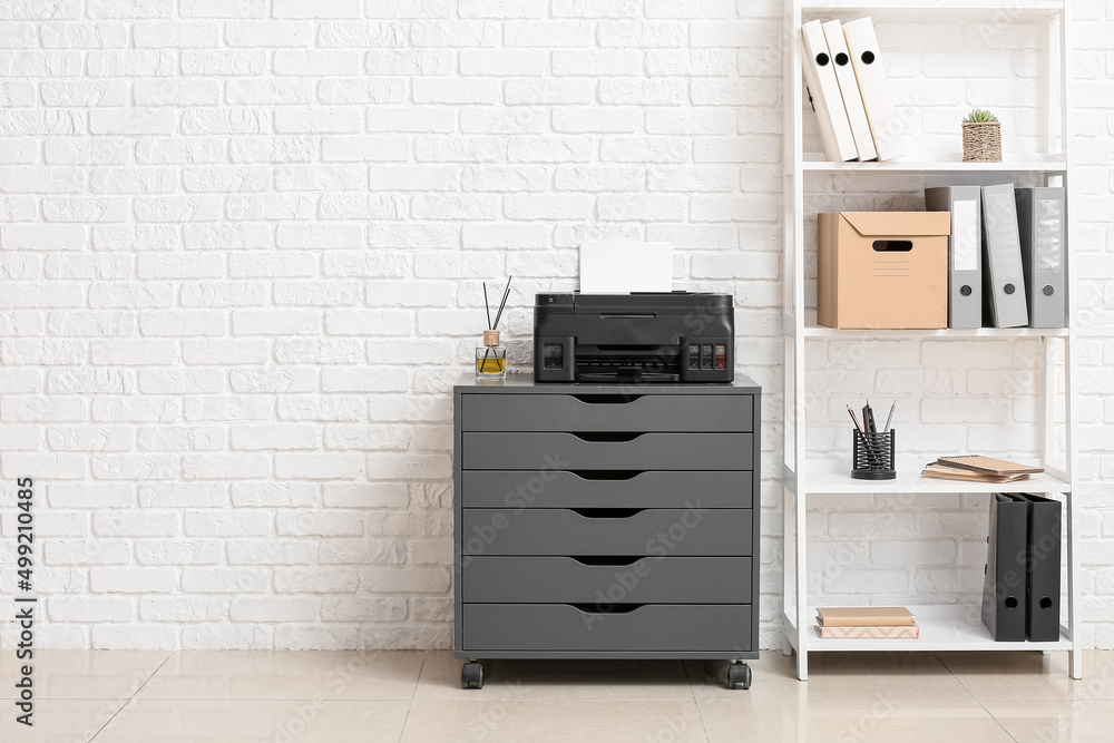 Chest of drawers with modern printer and shelf unit near white brick ...
