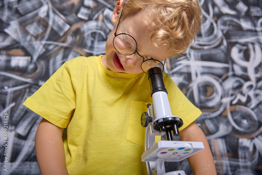 Closing one eye boy stares intently at eyepiece of microscope through ...