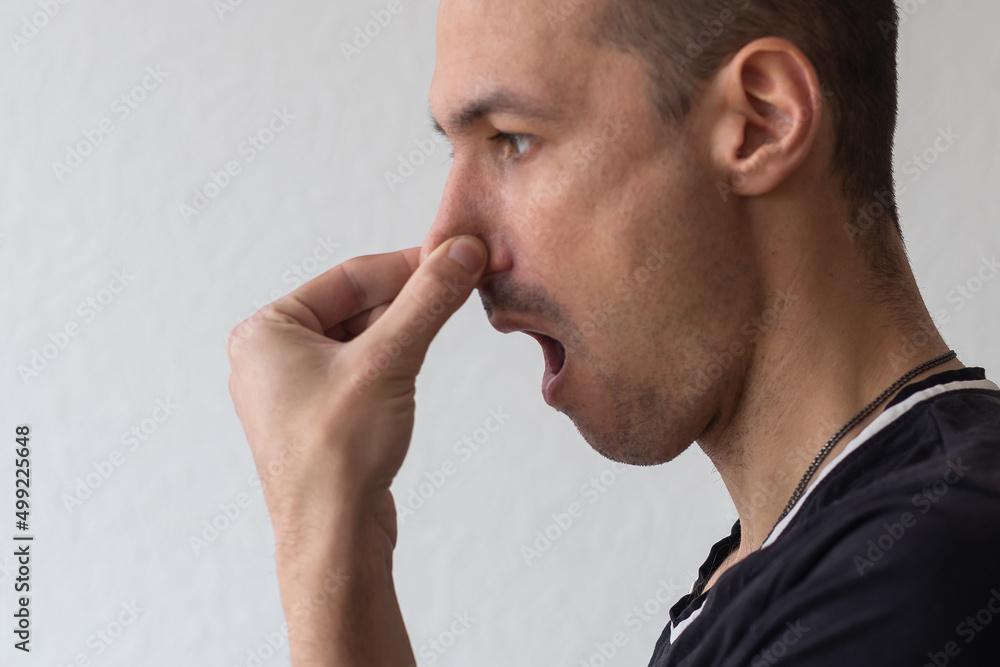 Man smells something stinky and pinches his nose to stop the bad odor ...