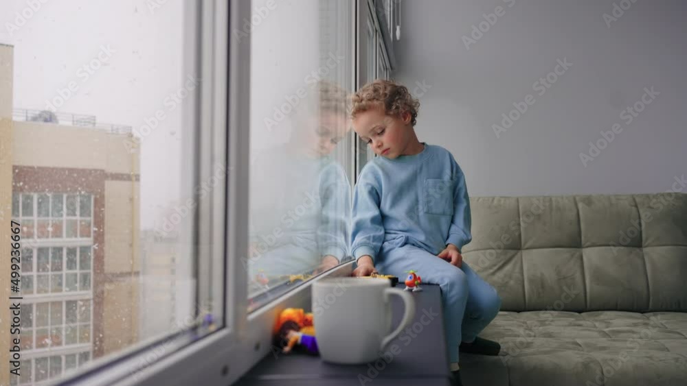 Vidéo Stock little boy is boring alone in room, looking out window in ...