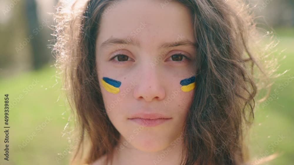 Close up portrait of serious girl with flag of Ukraine on face. Concept ...