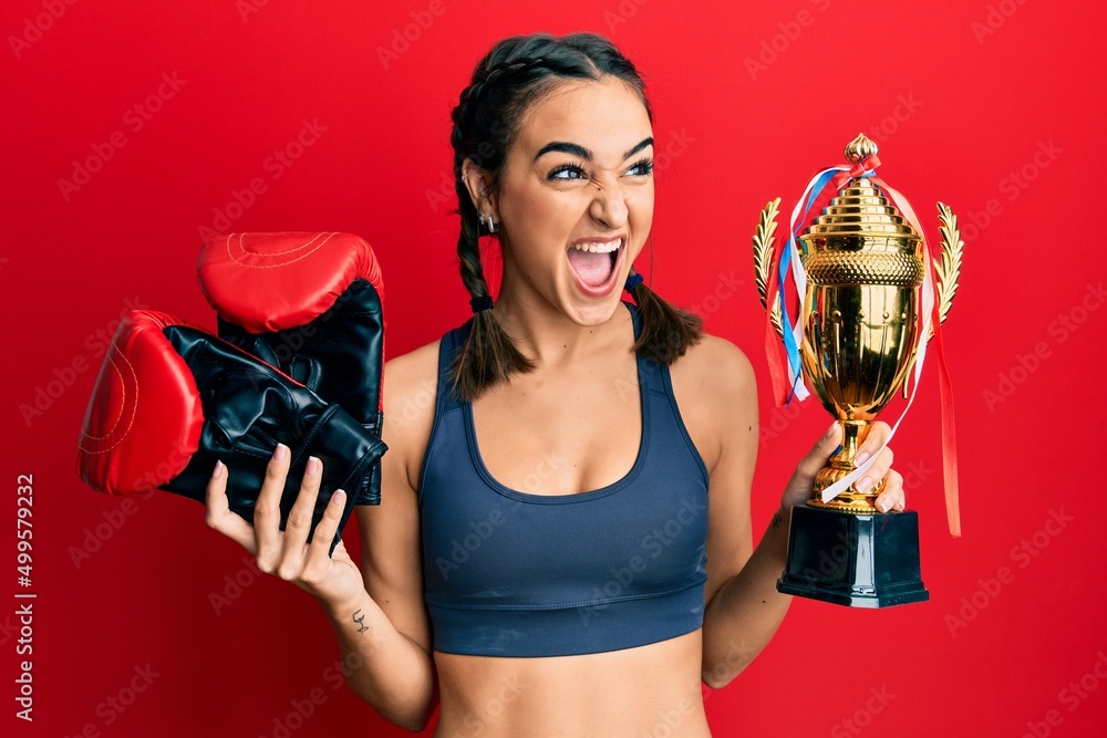 Foto de Young brunette girl holding boxer gloves and trophy angry and ...