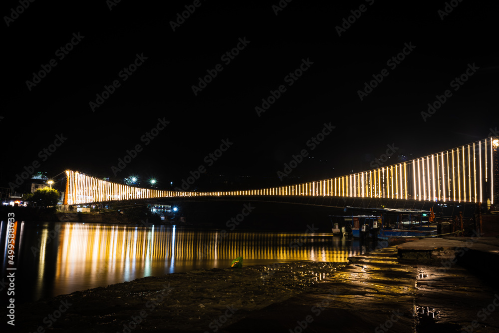iron suspension bridge illuminated with ferry lights with water ...