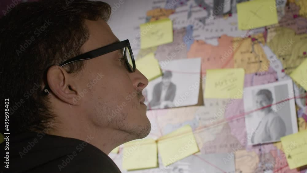 Caucasian young man looking at wall map with strings, stickers and ...