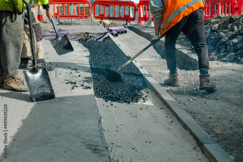 Construction workers placing hot tarmac after installation of new ...