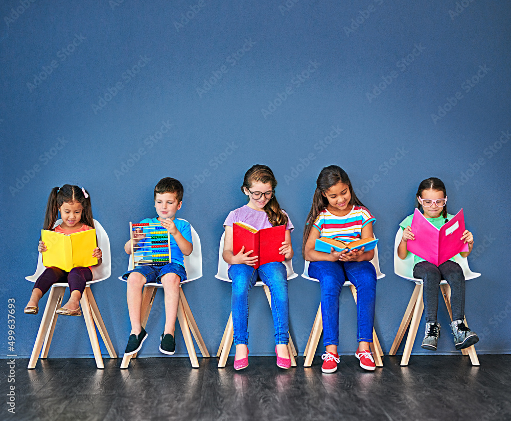 Lined up to learn. Studio shot of a group of kids sitting on chairs and ...