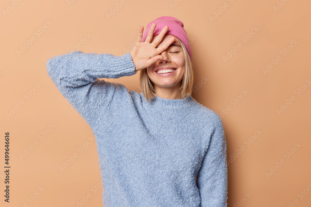 Indoor shot of cheerful pretty teenage girl keeps eyes closed covers ...