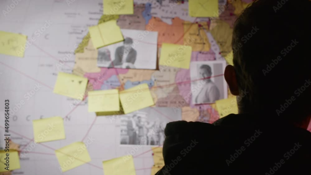 Caucasian young man looking at wall map with strings, stickers and ...