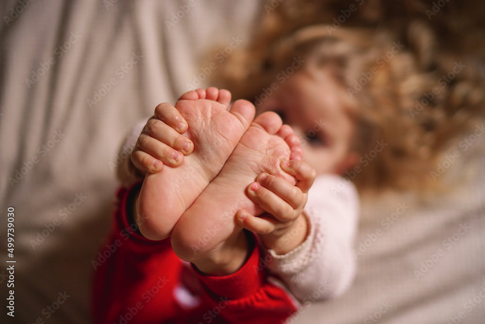 little girl holding her legs barefoot, baby feet close-up in focus ...