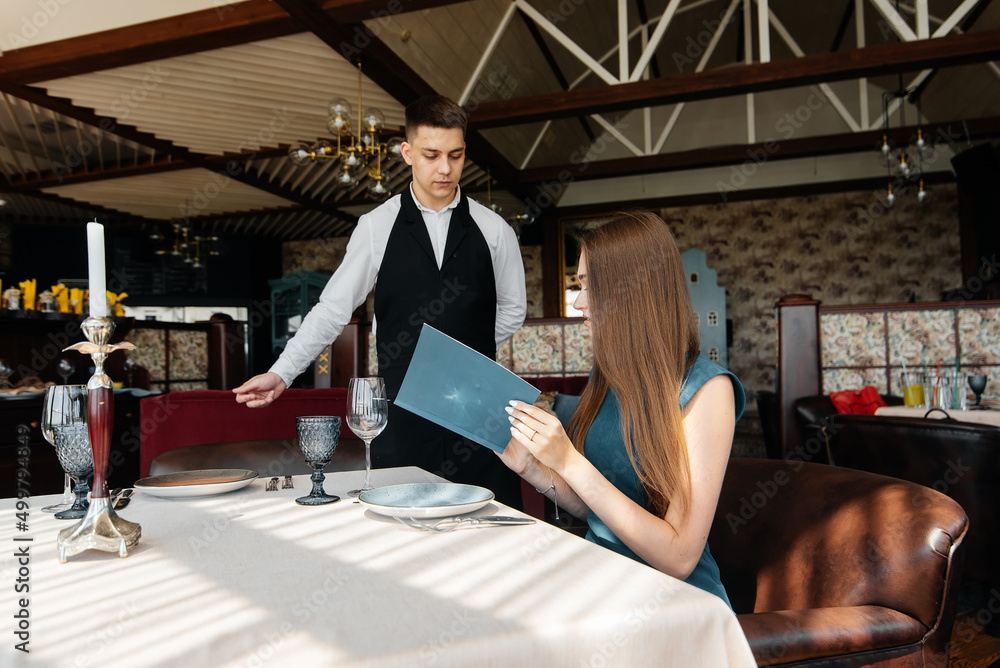A young beautiful woman in an elegant restaurant looks through the menu ...