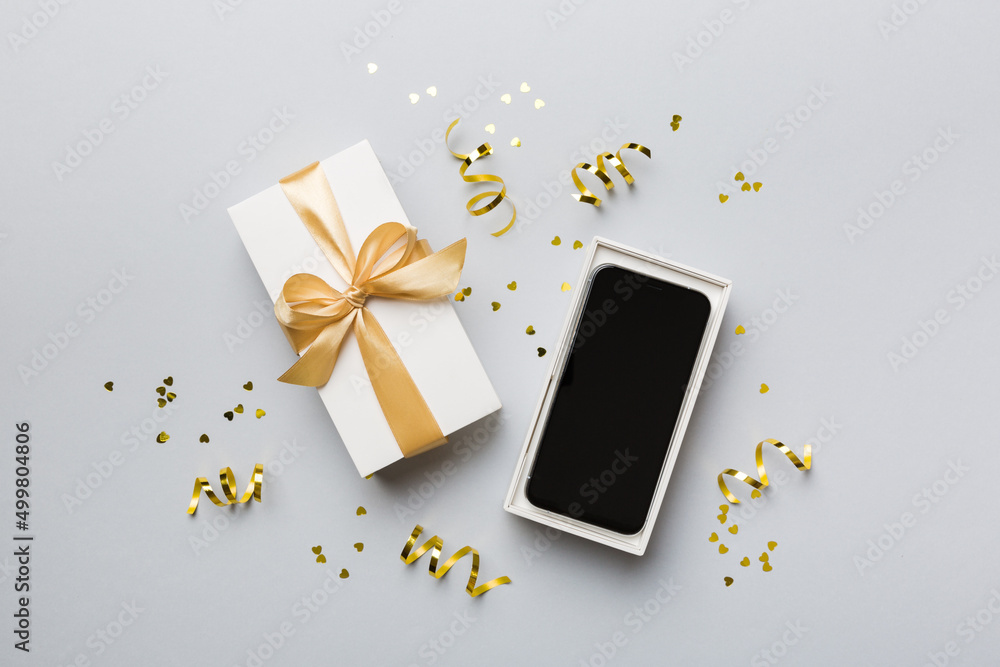 Opened gift box with gold ribbon and smartphone on color background ...