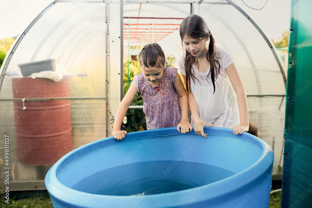 Wet happy children in the garden are bathing in a big blue barrel ...