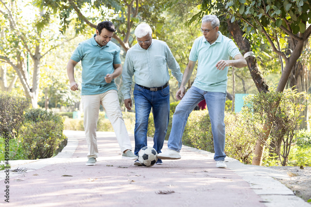 Two senior man with son having fun while playing football at park Stock ...