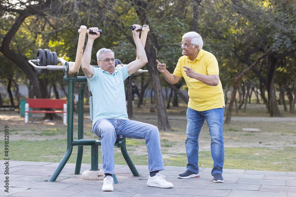 Two senior man having fun while exercising in open air gym at park ...