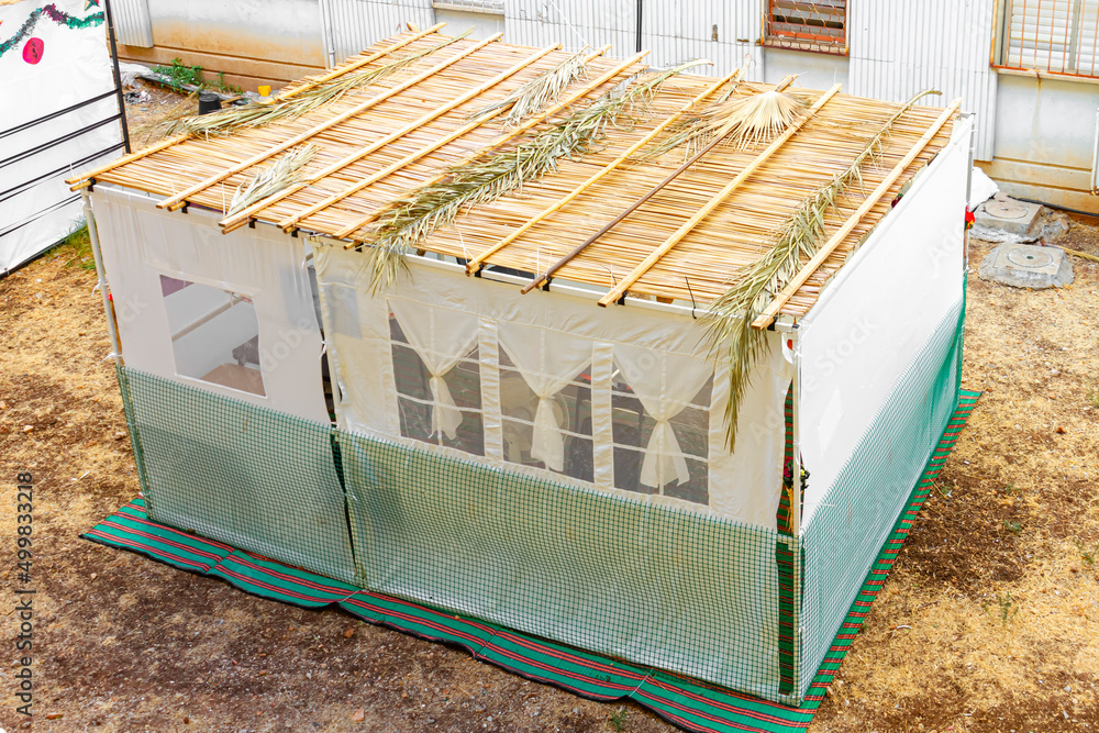 White Sukkah outside on the street with a garden and trees near the ...