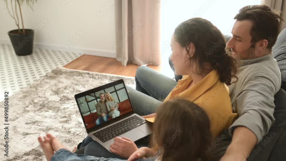 Family of four using laptop for video connection with grandparents or ...