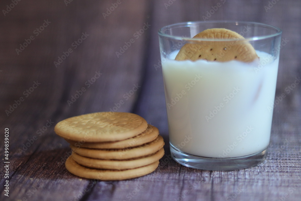Vaso de leche con galleta dentro y al lado un montoncito de galletas ...