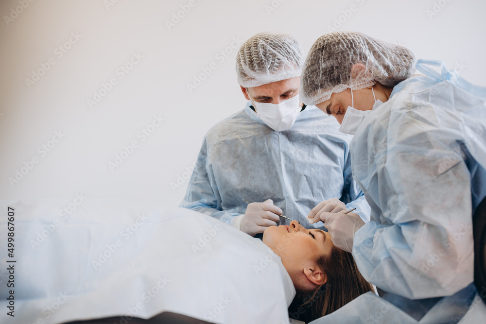 Surgeon and his assistant performing cosmetic surgery on nose in ...