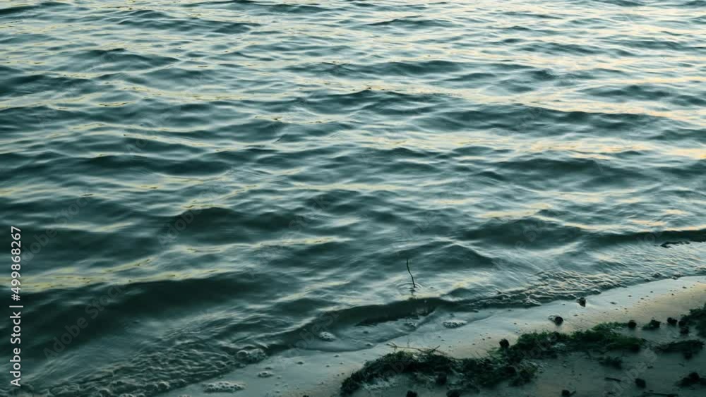 Ominous blue waves roll darkly on the dark sandy bank of the river ...