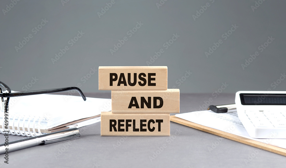 PAUSE AND REFLECT text on wooden block with notebook,chart and calculator, grey background Stock ...