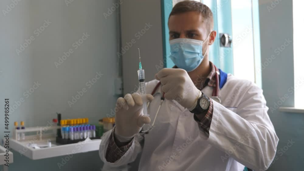 Male doctor in protective mask pouring liquid from syringe. Hospital ...