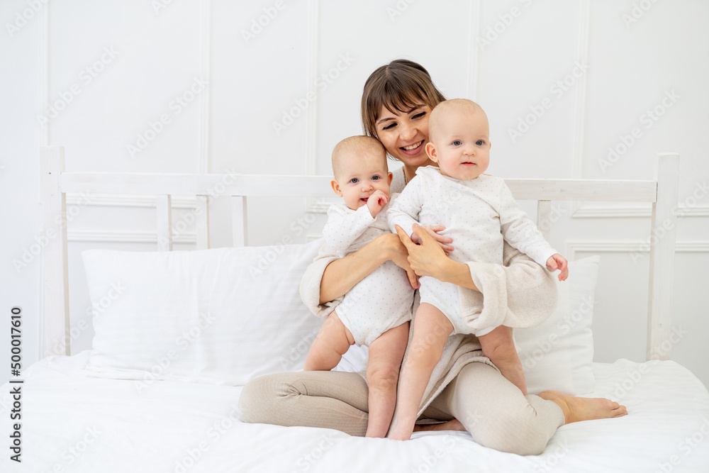happy mom with two twin babies at home on the bed hugging and kissing ...