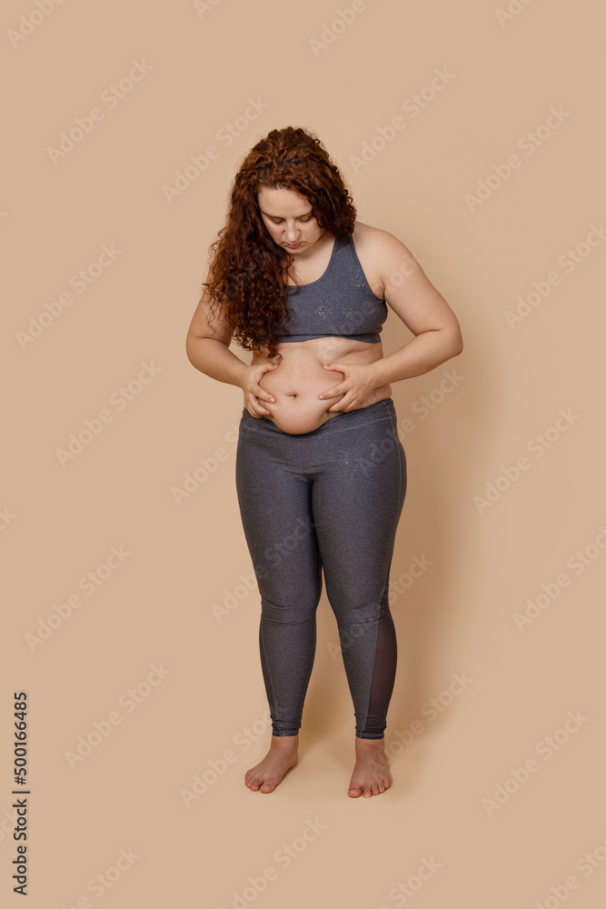 Vertical puzzled red haired overweight fat barefoot woman looking on ...
