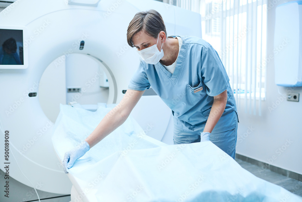 Short-haired nurse in surgical mask and gloves spreading out disposable ...