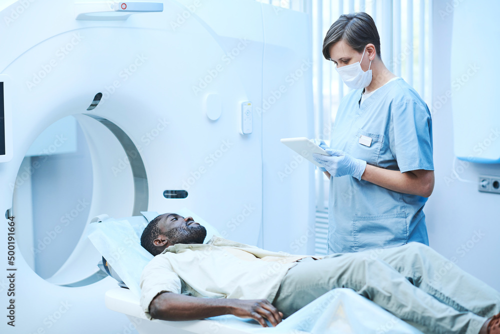 Caucasian nurse in scrubs and mask standing at MRI scanner and asking ...