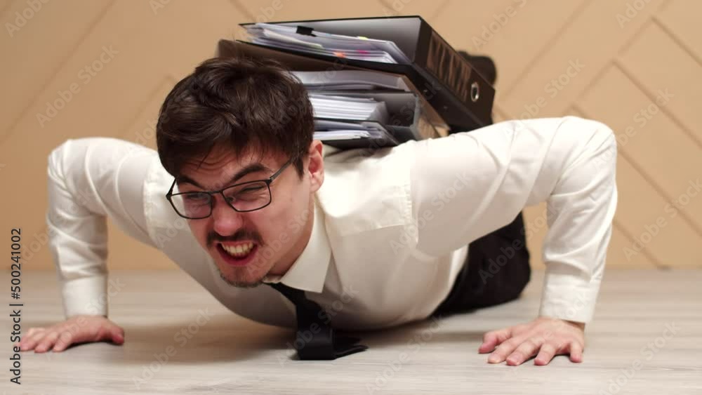 Male office worker is pinned down by stack folders of working documents ...