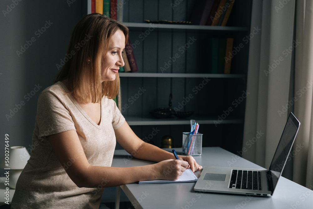 Side view of focused woman write making notes, studying online on ...