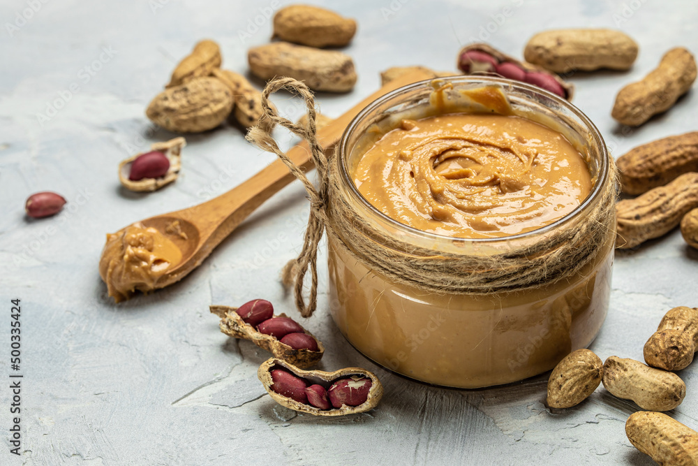 peanut paste in an open jar in spoon near creamy peanut butter peanuts ...
