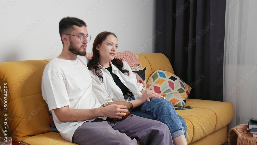 A Young Couple Is Sitting On The Couch Watching TV The Young Woman Had a-young-couple-is-sitting-on-the-couch-watching-tv-the-young-woman-had