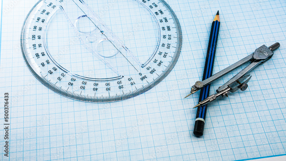On blue graph paper are compasses, protractor, ruler, and a pencil ...