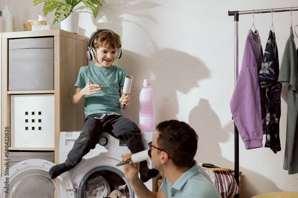 Baby sits on the washing machine while dad puts the laundry in. The ...